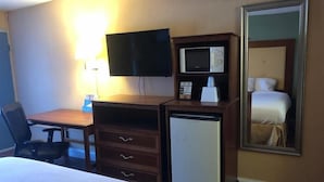 Quarto de hotel com cama, escrivaninha, cadeira, televisão, micro-ondas, frigorífico e espelho.