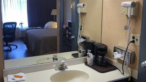 Casa de banho de hotel com um espelho grande, uma pia, uma máquina de café e um secador de cabelo.