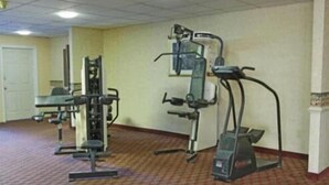 Sala de ginástica com equipamentos de cardio e musculação, piso coberto de carpete e uma porta ao fundo.