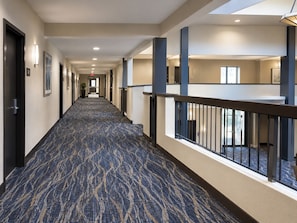 Corredor de hotel com carpete estampado, portas e corrimão com vista para um andar inferior.