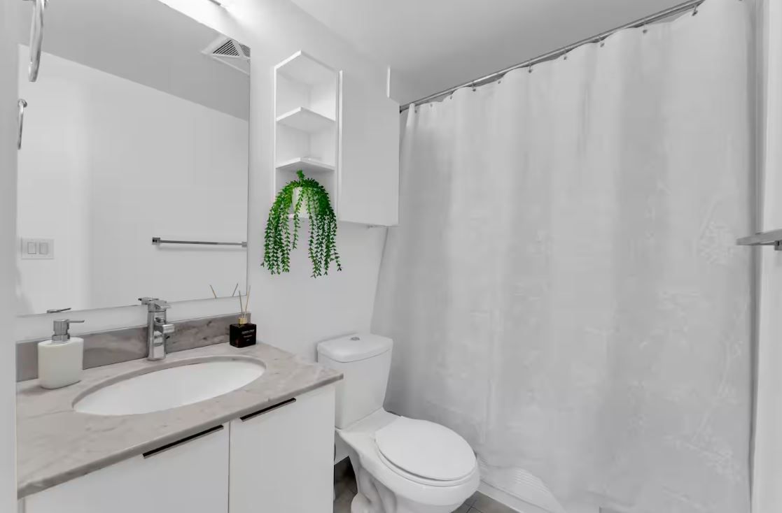 Casa de banho com lavatório branco, espelho e sanita.