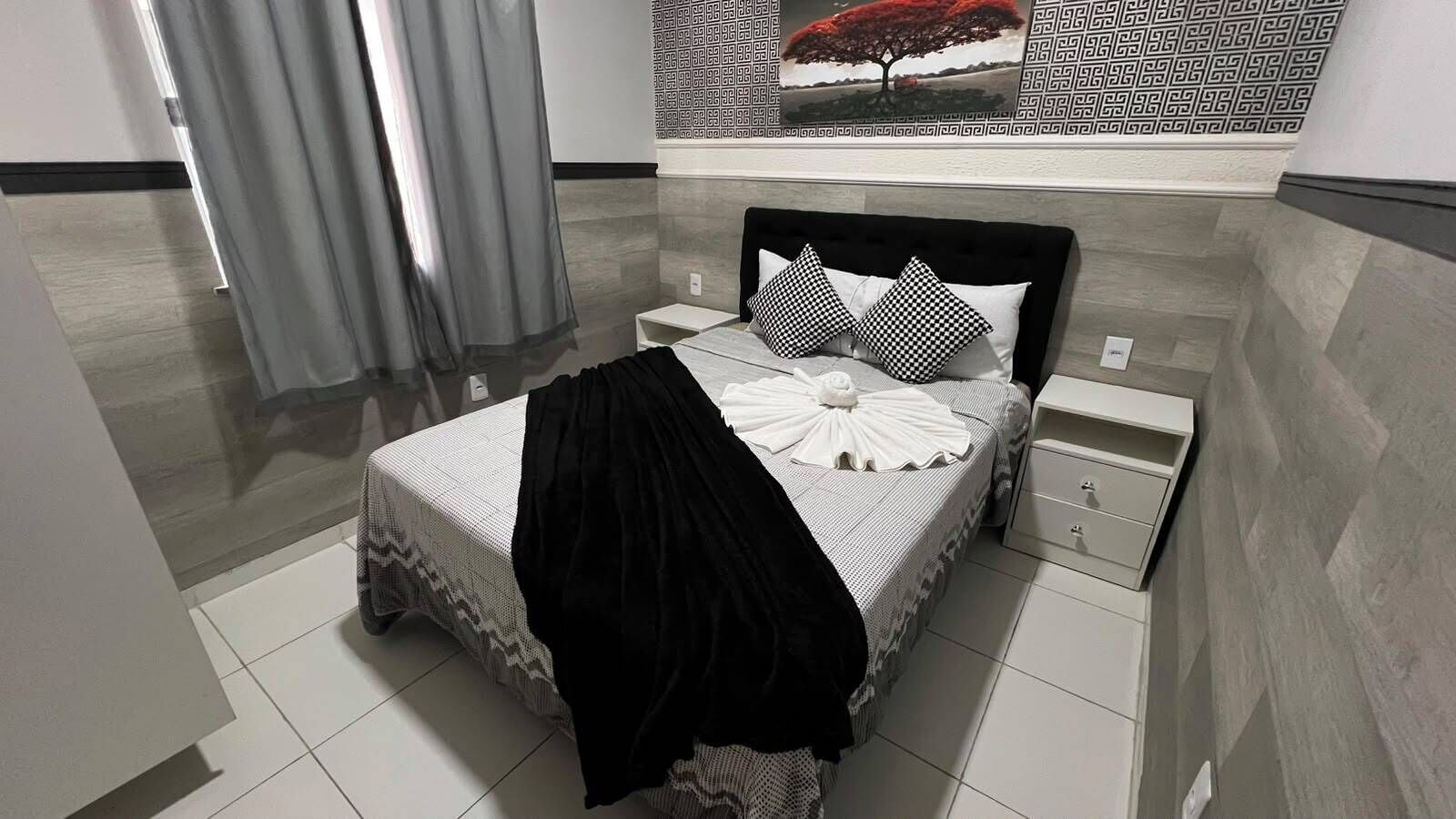 Quarto com cama, mesas de cabeceira, cômoda e parede com padrão geométrico.