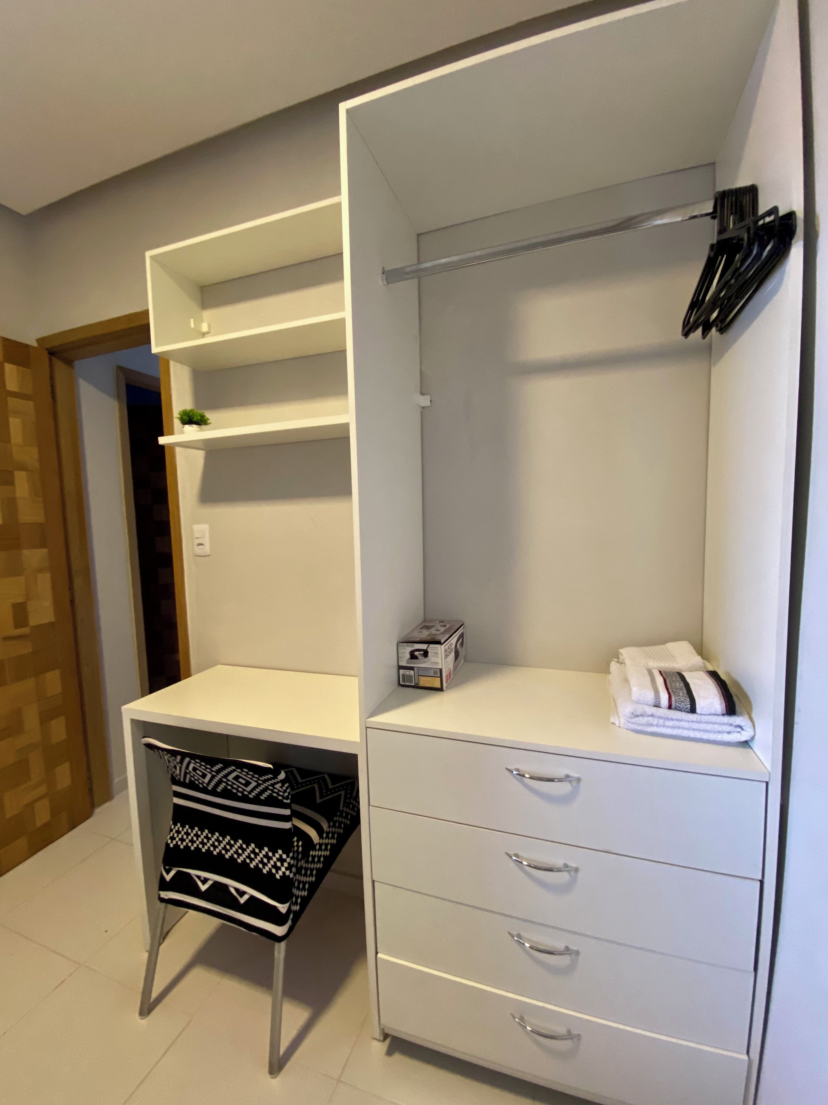 Guarda-roupa branco com três gavetas e barra para pendurar roupas.