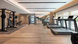 Uma academia equipada com aparelhos de cardio, máquinas de musculação e um espelho grande.