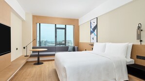 Quarto de hotel moderno com uma cama grande, área de estar, TV de tela plana e vista para a cidade.