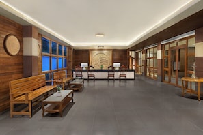 Área de recepção com bancos de madeira, balcão de atendimento e um grande emblema fixado na parede.