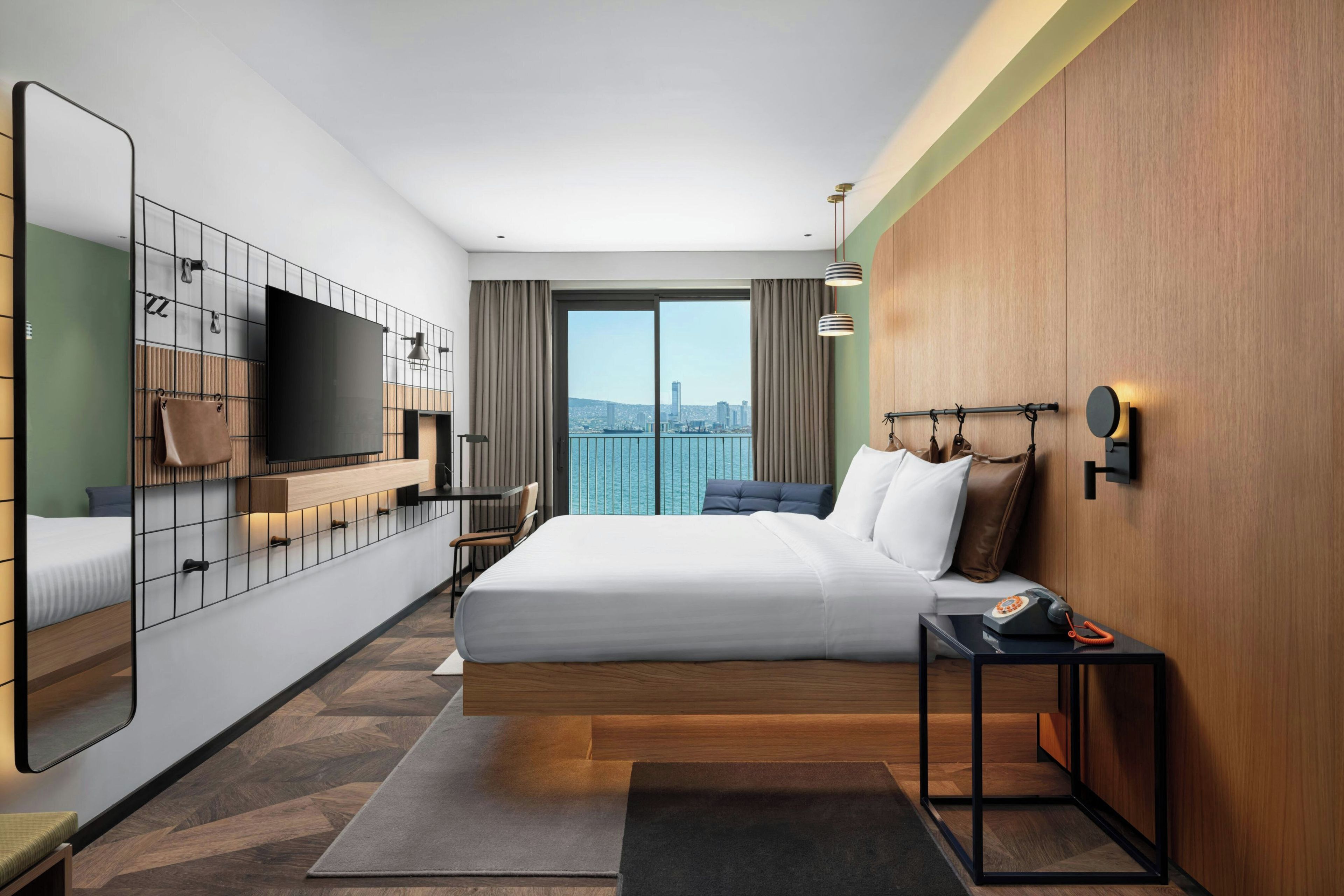 Quarto de hotel moderno com uma cama grande, televisão, escrivaninha e vista para a cidade.