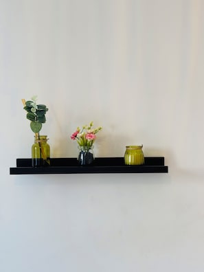 Uma prateleira preta com três vasos de vidro contendo plantas e flores.