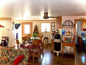 Uma sala de estar com um sofá estampado, um espaço de jantar com mesa e cadeiras, uma cozinha com armários e eletrodomésticos, e um ventilador de teto.