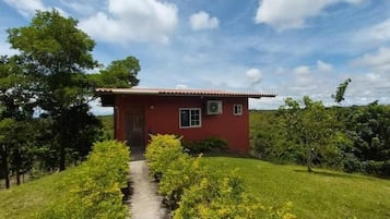 Uma casa térrea vermelha com telhado de cerâmica, rodeada por vegetação e árvores.
