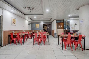 Uma área de refeições de hotel com cadeiras e mesas vermelhas, um ventilador de teto e uma placa com a inscrição 'KASIR HOTEL'.