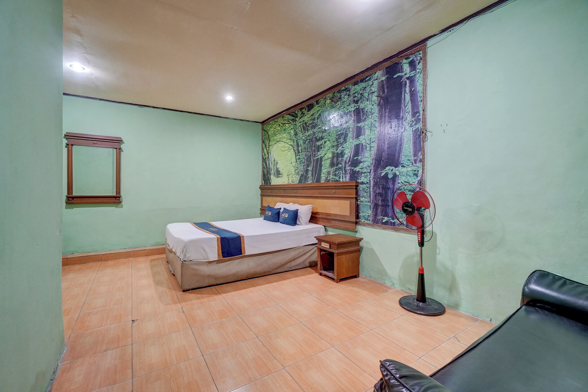 Quarto com cama, mesa de cabeceira, ventoinha, janela e parede com mural de floresta.