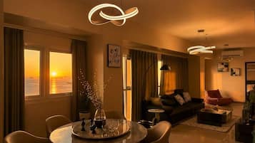 Uma sala de estar moderna com área de jantar, amplas janelas com vista para o pôr do sol e luminárias contemporâneas.