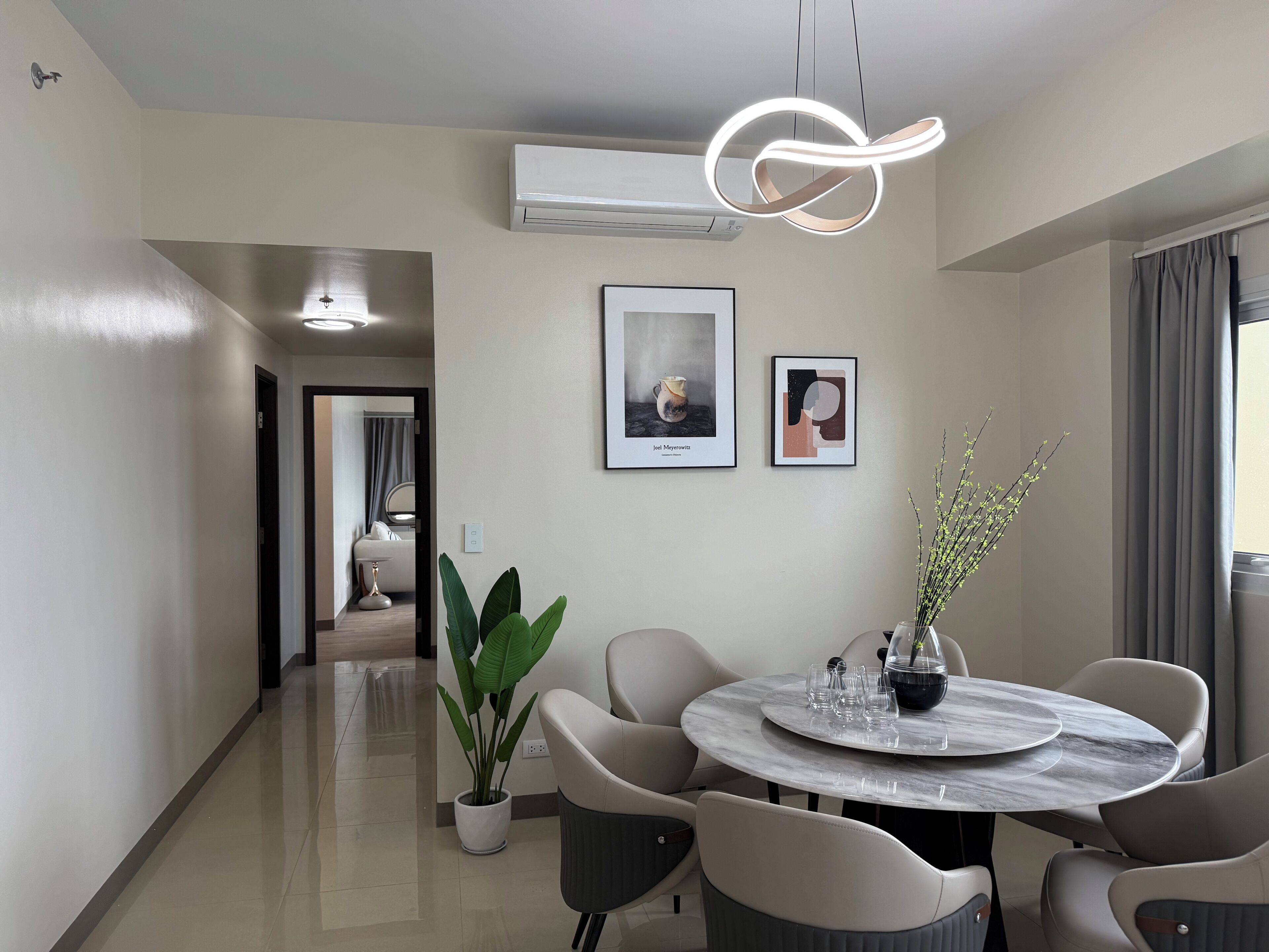 Uma sala de jantar moderna com uma mesa redonda, cadeiras, um vaso de planta e obras de arte na parede.