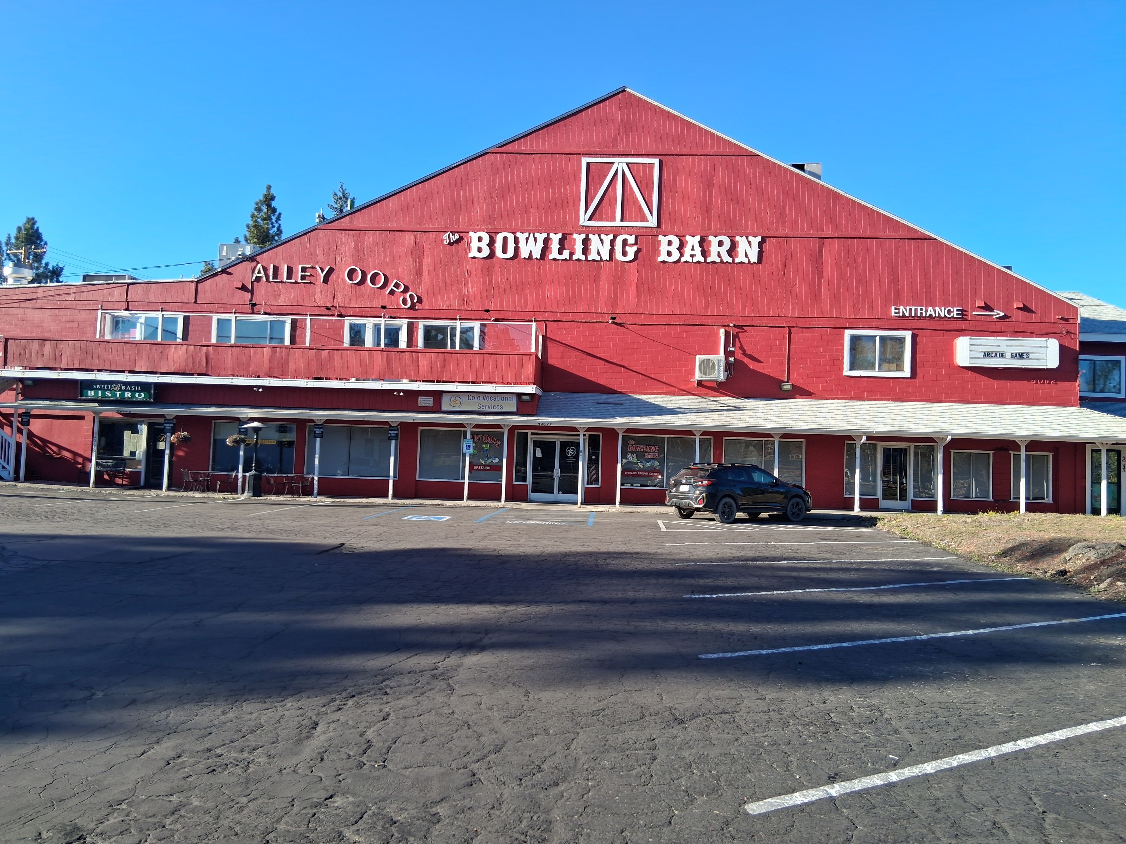Um edifício vermelho com a placa 'BOWLING BARN', uma loja chamada 'ALLEY OOPS BISTRO' e um carro estacionado em frente.