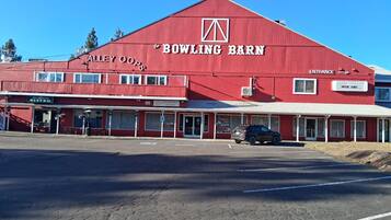 Um edifício vermelho com a placa 'BOWLING BARN', uma loja chamada 'ALLEY OOPS BISTRO' e um carro estacionado em frente.