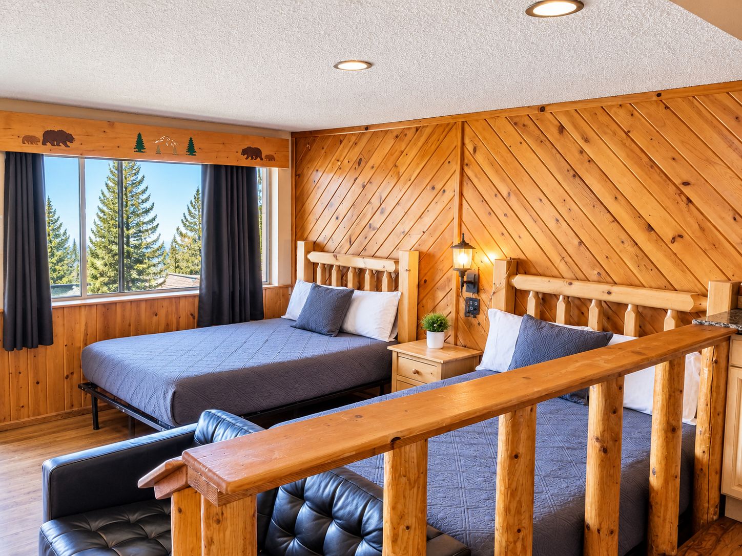 Quarto no estilo cabana com duas camas, cabeceira de madeira, mesa de cabeceira com abajur e vista para as árvores pela janela.