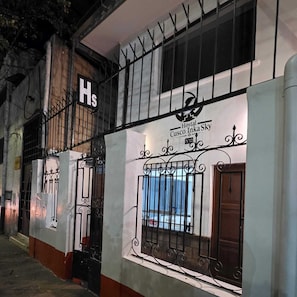 Um edifício com janelas protegidas por grades e uma placa indicando que se trata de um albergue chamado 'Hostal Cusco Inka Sky'.