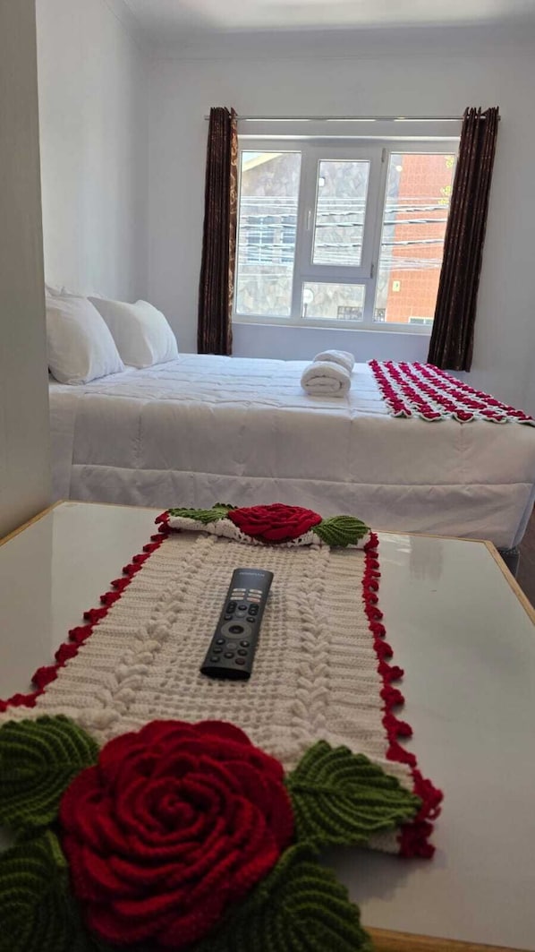 Quarto de hotel com cama, mesa com controle remoto e vista para o exterior.
