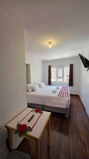 Quarto de hotel com cama, mesa com controle remoto, televisão na parede e janela com cortinas.