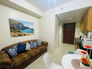 Um espaço compacto com sofá, mesa de jantar com cadeiras, cozinha e uma porta que dá para outro quarto.