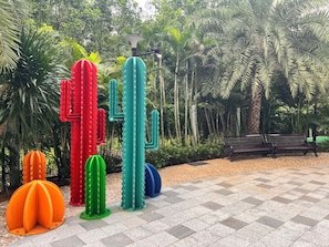 Uma área pavimentada com um banco e esculturas de cactos coloridos.