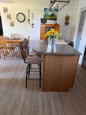 Cozinha com ilha central, cadeiras de madeira, mesa de jantar e utensílios de cozinha fixados na parede.