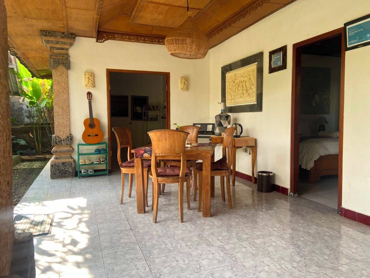 Um quarto com uma mesa de jantar e cadeiras, uma guitarra, e uma cama no quarto vizinho.