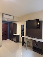 Quarto com escrivaninha, cadeira, guarda-roupa e televisão na parede.