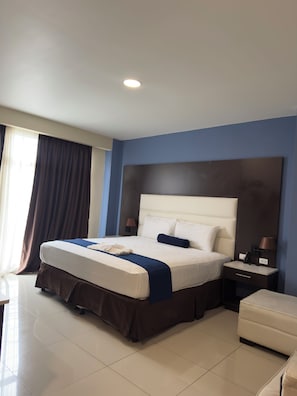 Quarto de hotel com uma cama grande, mesas de cabeceira, escrivaninha e uma cadeira.