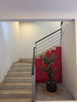 Escada com corrimão de metal, parede em destaque vermelha e planta em vaso com flores vermelhas.
