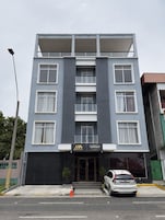 Um hotel com vários andares, fachada moderna, porta de garagem preta e um carro branco estacionado em frente.