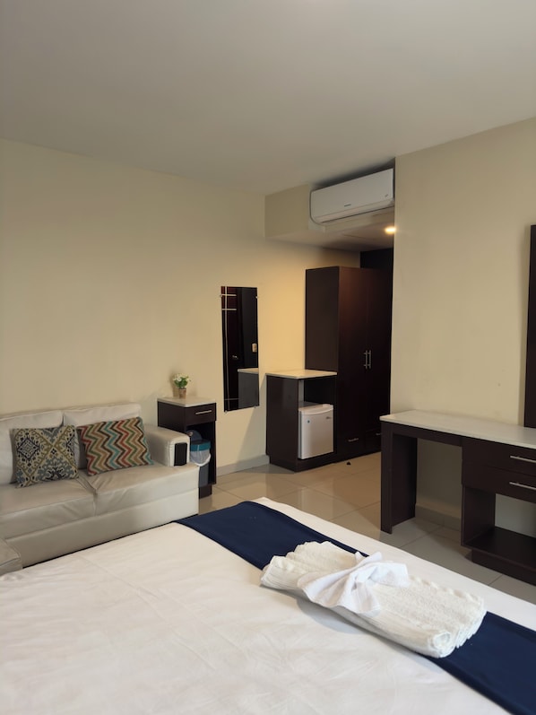 Quarto de hotel com cama, escrivaninha, guarda-roupa e uma pequena cozinha.