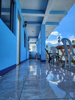 Um corredor com paredes azuis e chão de azulejos que leva a uma área de estar com cadeiras de plástico e uma mesa.