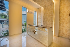Uma área de recepção com balcão de vidro, mesa de atendimento e parede com padrão.
