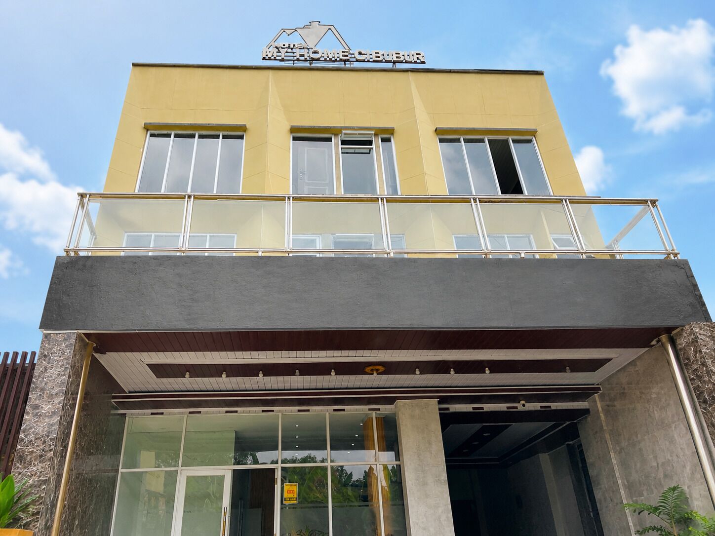 Um hotel com fachada amarela, varanda com guarda-corpos de vidro e uma placa sobre a entrada.