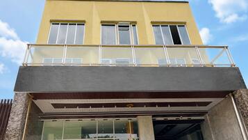 Um hotel com fachada amarela, varanda com guarda-corpos de vidro e uma placa sobre a entrada.