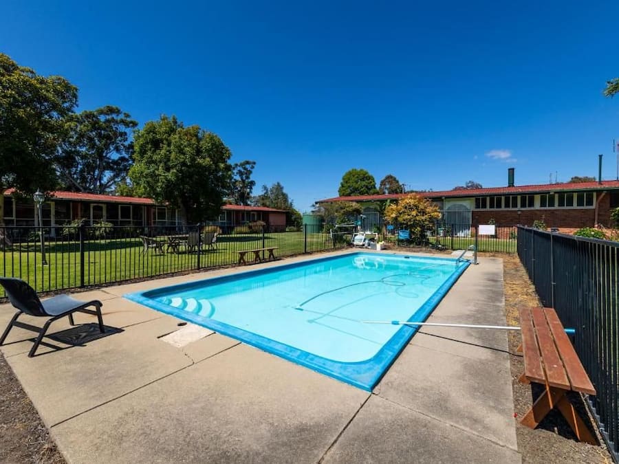 Uma piscina com quadra de basquete, cercada por grade, bancos e árvores.