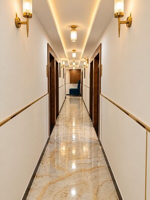 Corredor de hotel com piso de mármore, arandelas e uma cadeira azul.