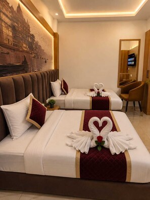 Quarto de hotel com duas camas, cada uma com arrumação de toalhas em formato de coração e almofada acolchoada vermelha.