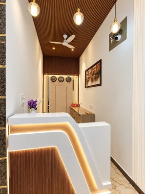 Uma área de recepção com design moderno, com balcão de atendimento, ventoinha no teto, relógios na parede e um quadro emoldurado.