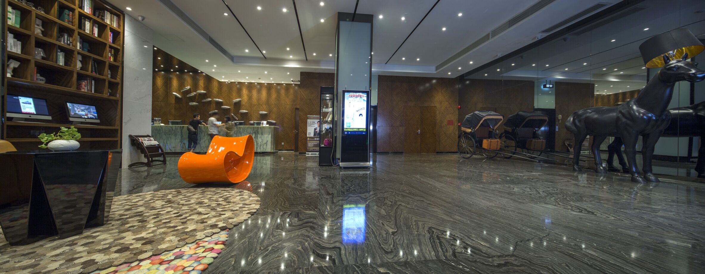 Um lobby moderno com balcão de recepção, área de estar e uma grande tela digital.