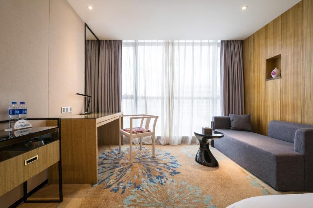Quarto de hotel com escrivaninha, cadeira, sofá e tapete decorativo.