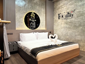 Quarto de hotel moderno com uma cama, uma mesinha de cabeceira, um relógio de parede e um logotipo circular na parede.