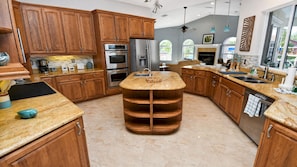 Uma cozinha com armários de madeira, uma ilha central, eletrodomésticos de aço inoxidável e vista para o exterior.