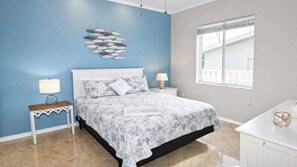 Quarto com uma cama, duas mesas de cabeceira, uma janela e um objeto decorativo na parede.