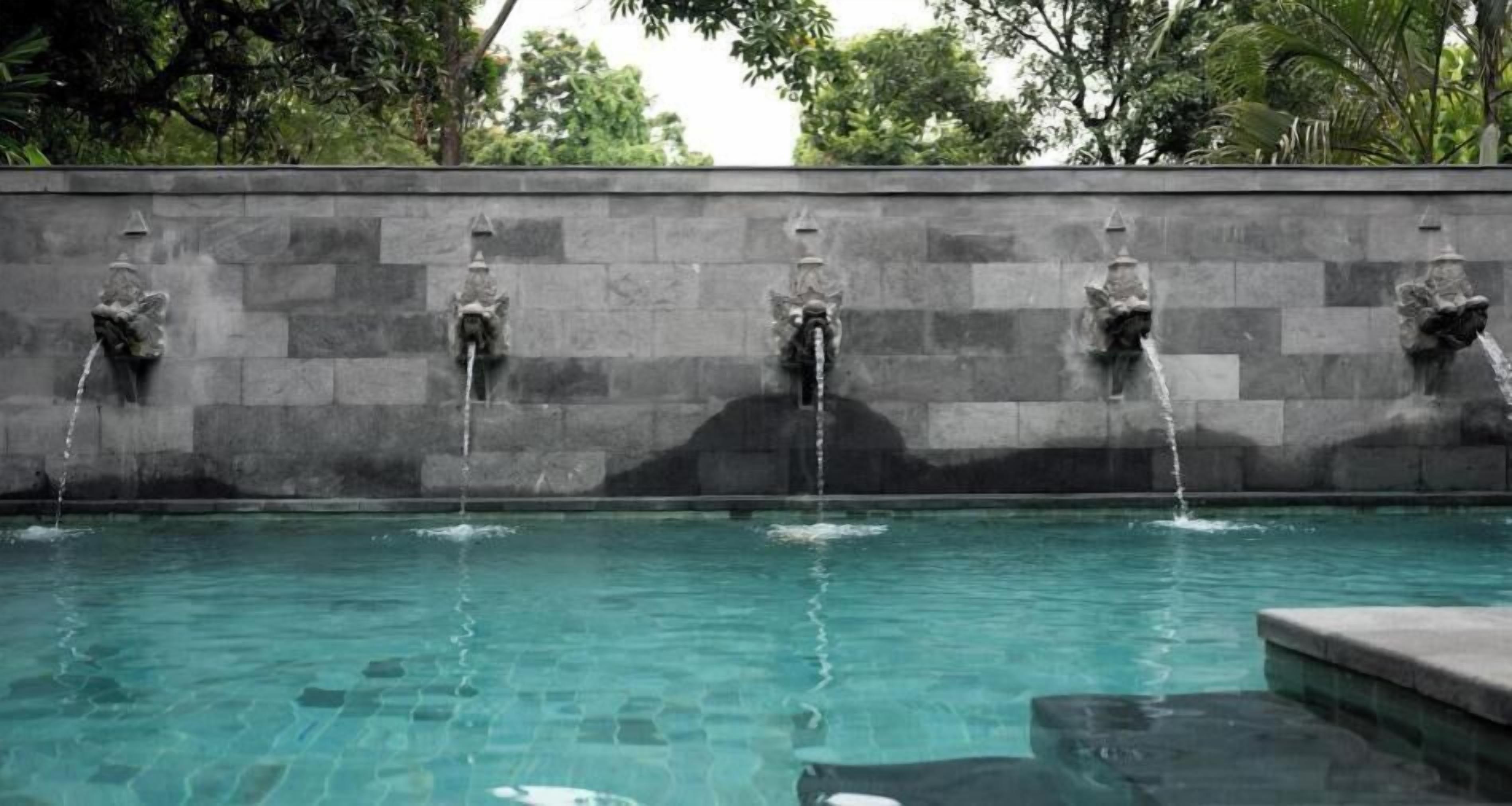Piscina com quatro bicos de água e uma parede de pedra.
