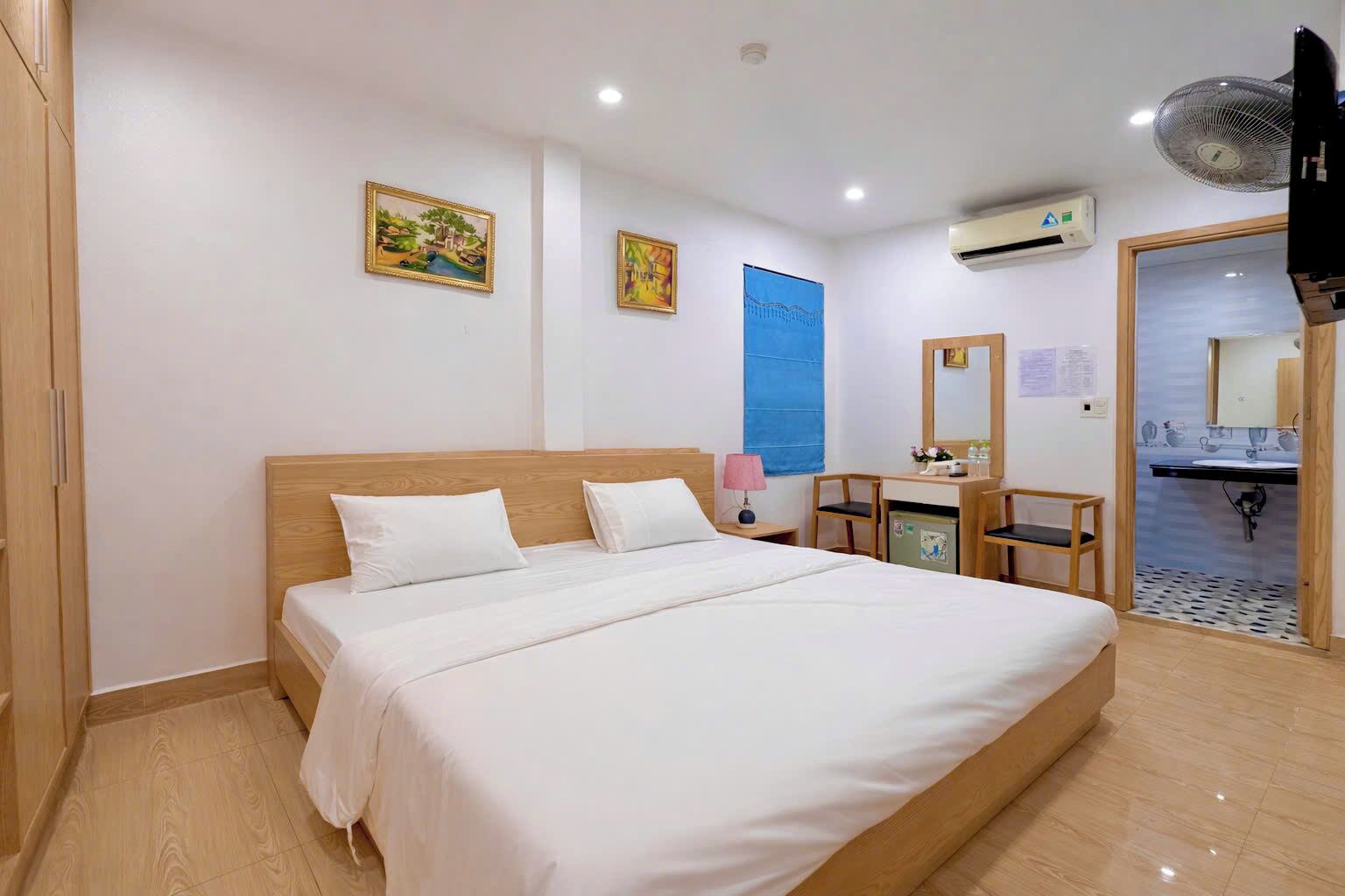 Quarto de hotel com cama de madeira, uma escrivaninha, cadeira, espelho e ar condicionado.