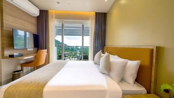 Quarto de hotel com uma cama grande, uma escrivaninha com cadeira, televisão e varanda com vista para o exterior.