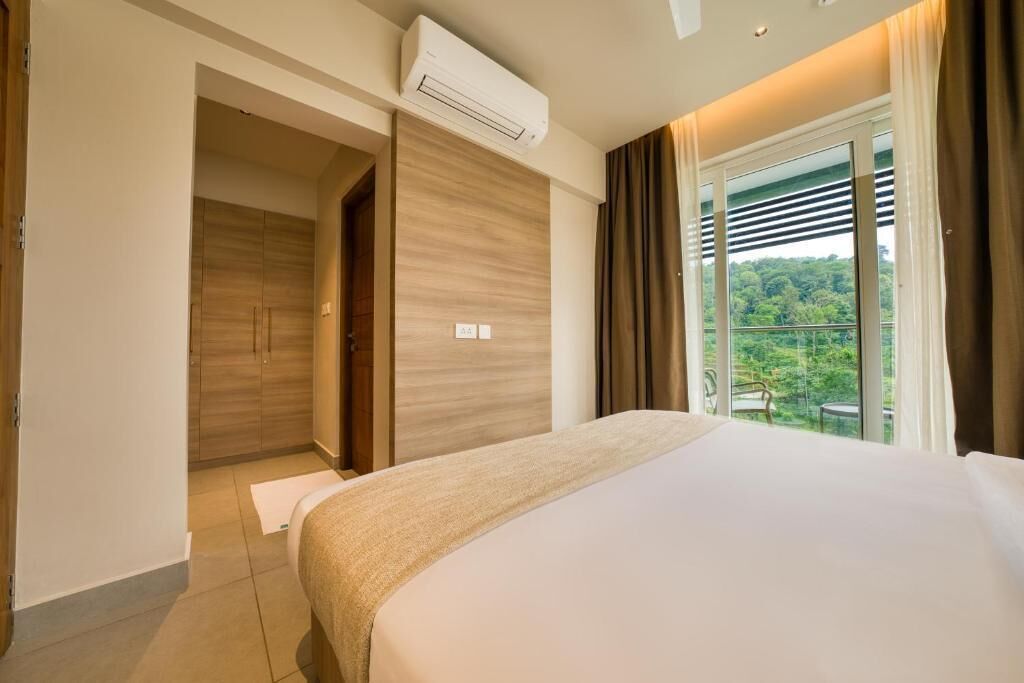 Quarto de hotel com cama, ar condicionado, porta deslizante e varanda com vista para o verde.